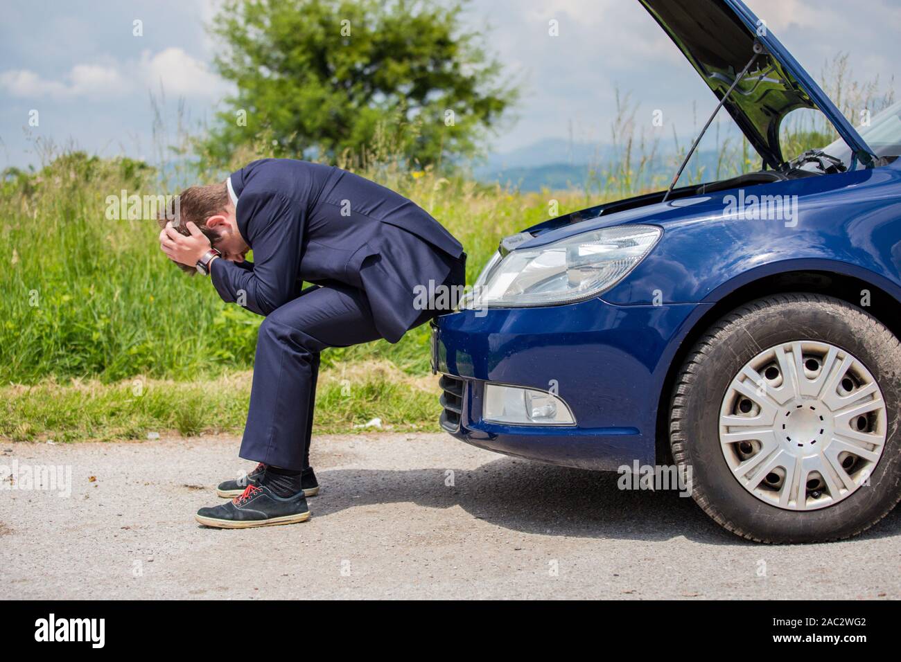 A broken car on the road, the driver is holding his head, an open hood ...