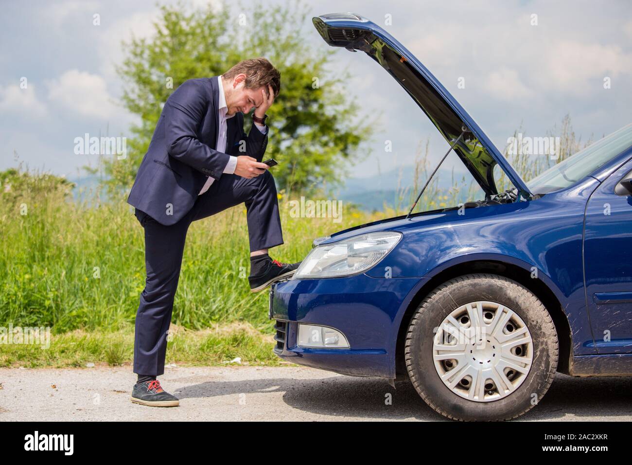 A broken car on the road, the driver is holding his head, an open hood ...