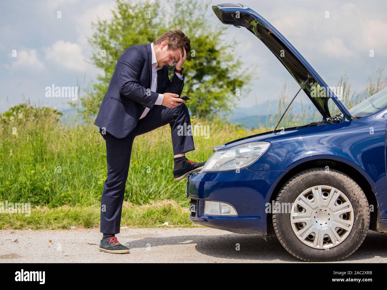 A broken car on the road, the driver is holding his head, an open hood ...