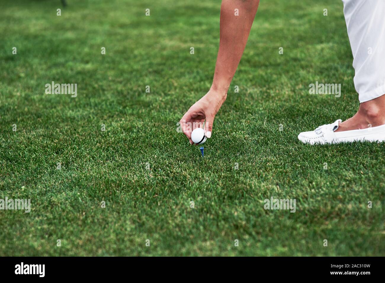 Female hand putting golf ball on the pin standing in the green field ...