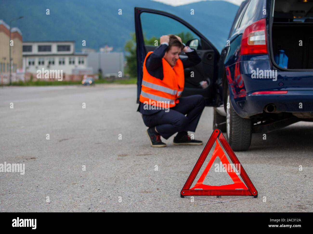 A broken car on the road, the driver is holding his head, an open hood ...