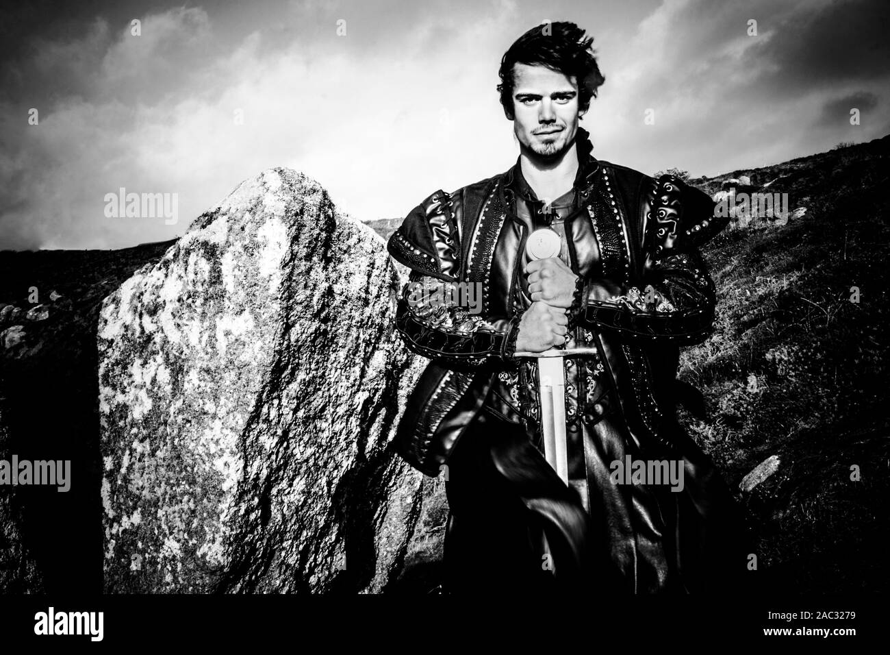 Portrait of handsome knight in costume standing next to rock holding ...