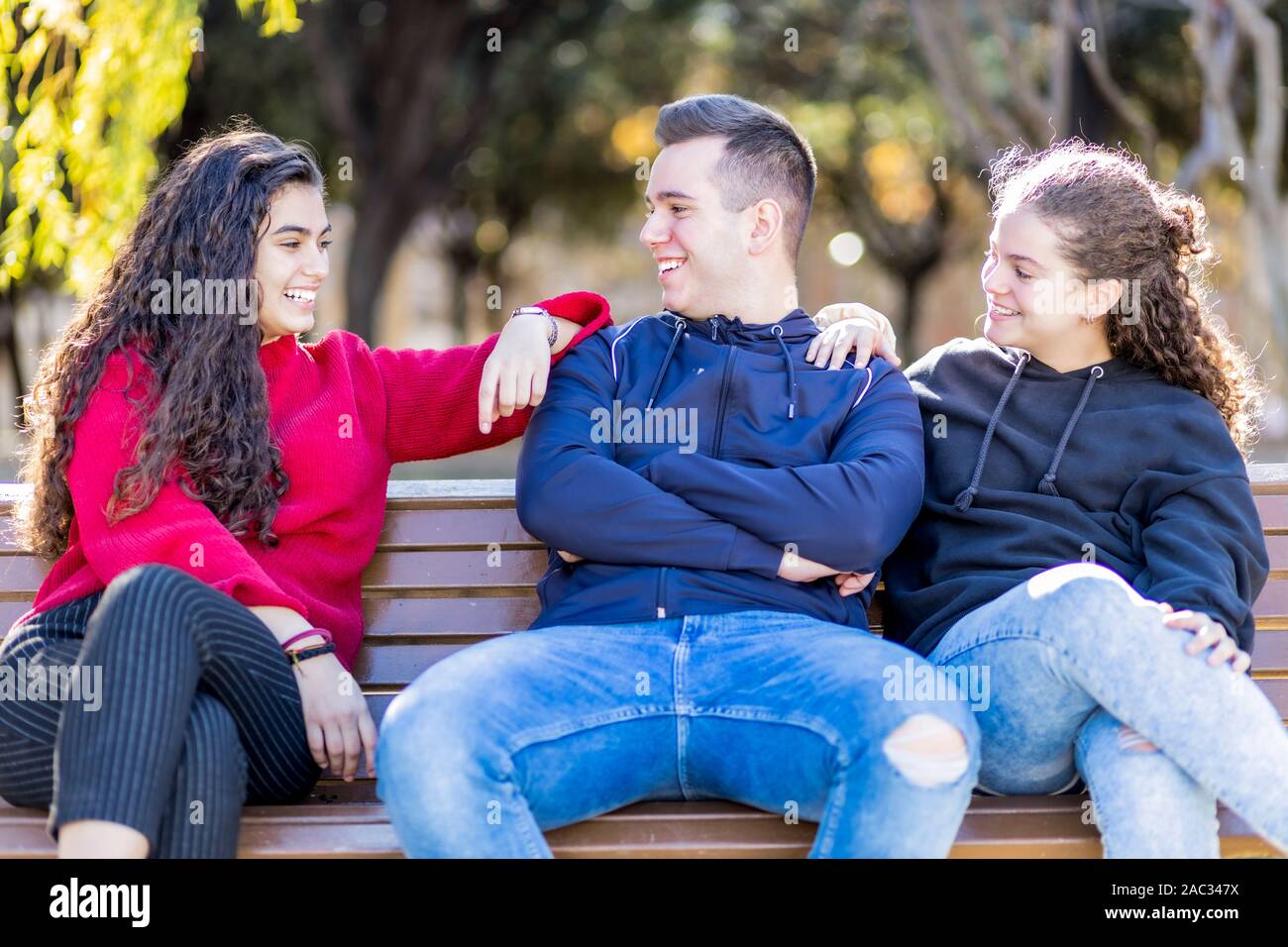 Three friends talking and laughing on a park bench Stock Photo - Alamy