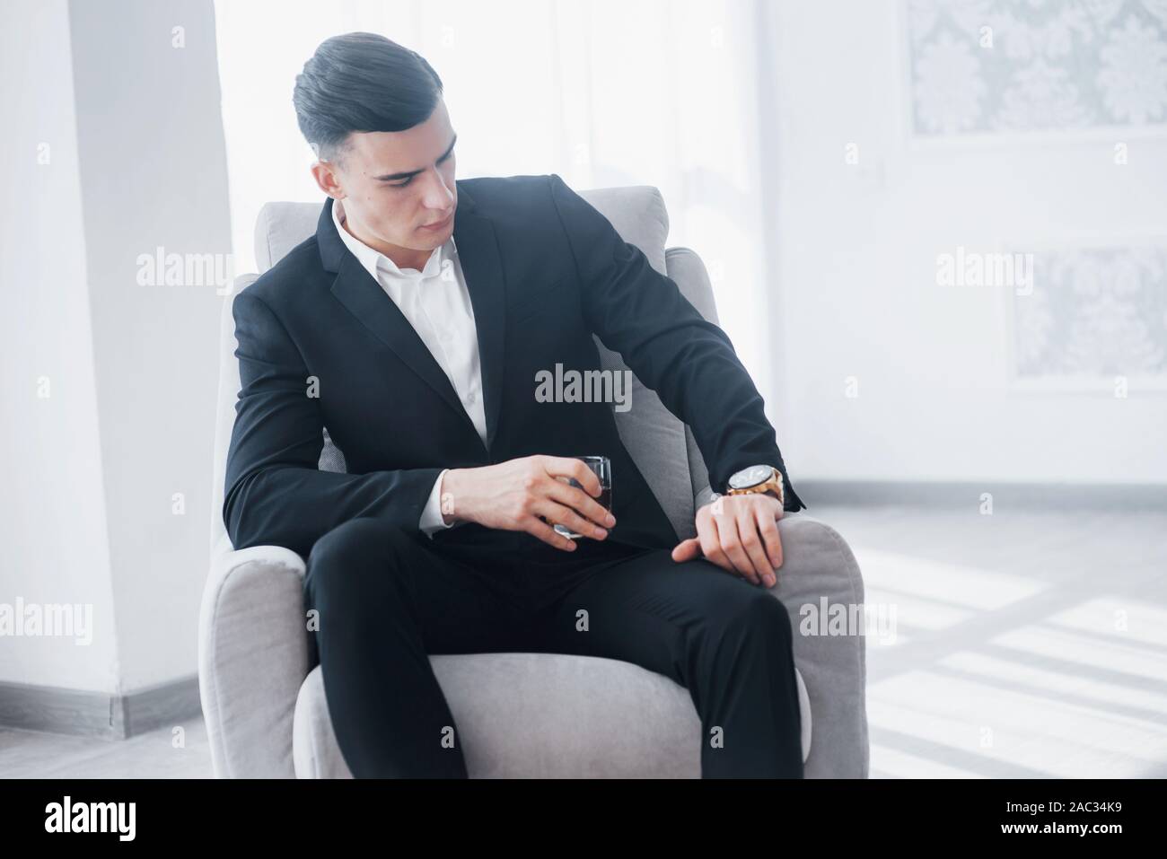 Checks the time on luxury watch. Young elegant guy in black suit ...