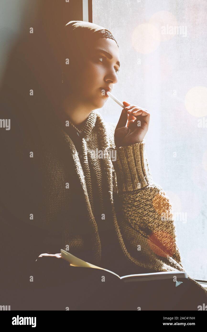 Young Muslim woman sits on the window sill. Middle-eastern writer woman ...