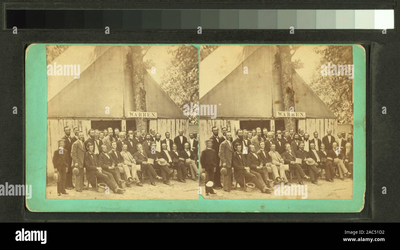 Group of men formally posed in front of large tent with sign that reads ...
