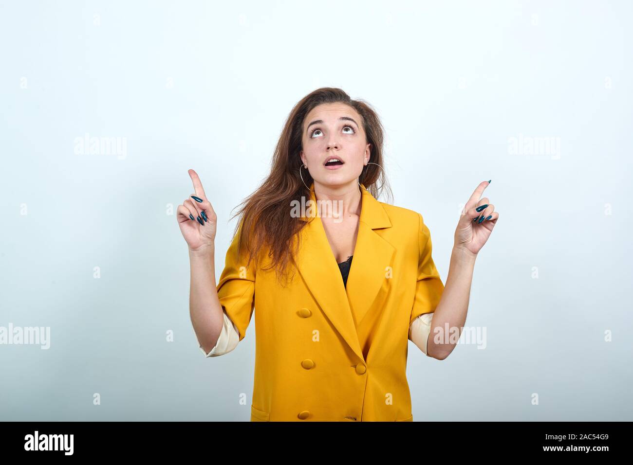 Pretty young woman in yellow jacket looking up, pointing into distance ...