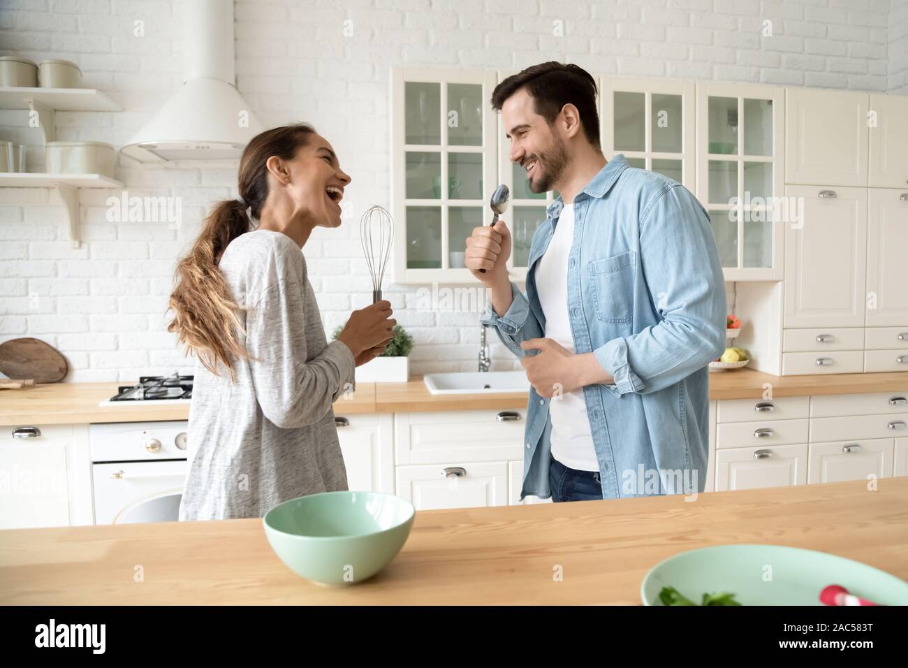 Funny couple singing in kitchenware microphones having fun in kitchen ...