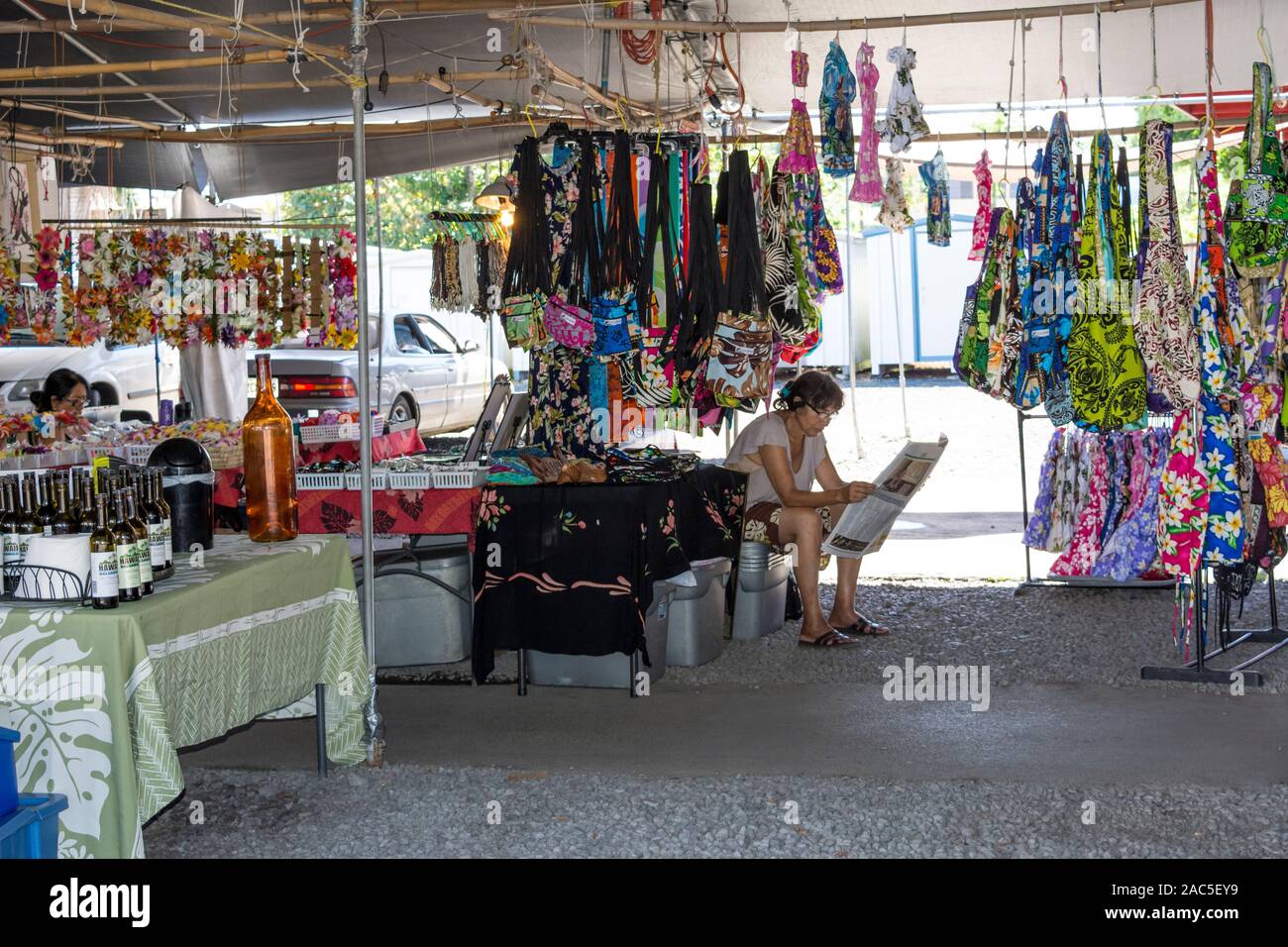A local fabric vendor reads a newspaper at the Hilo Farmers Market on ...