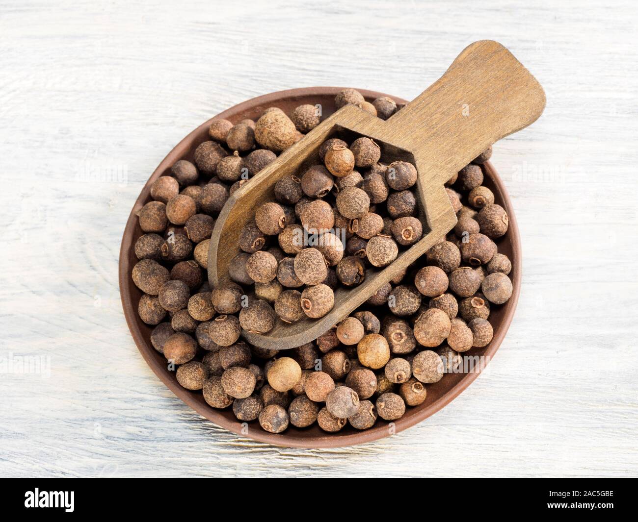 Allspice in clay plate and wooden scoop on a white background. Indian ...