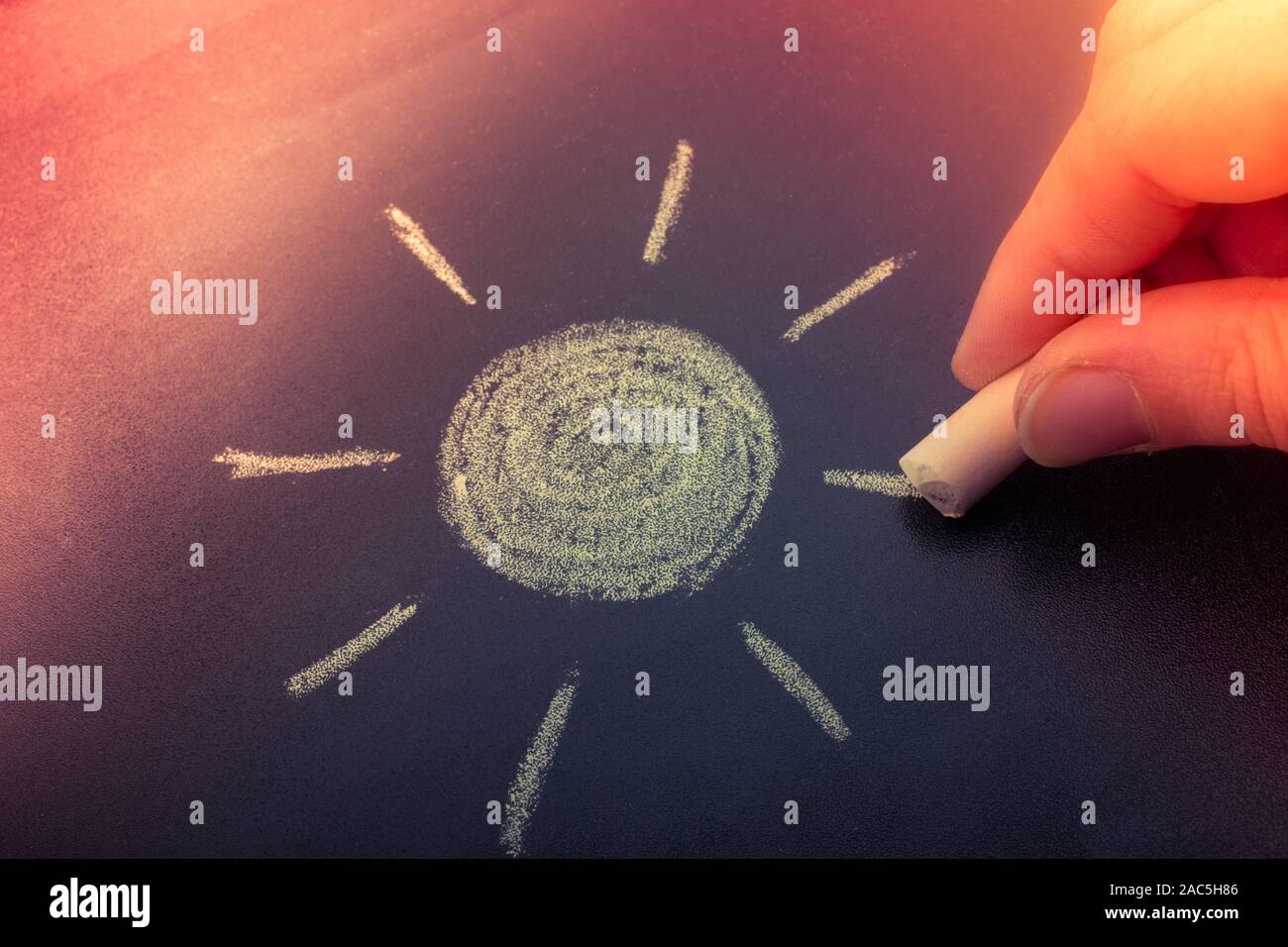 Hand drawing sun by chalk with light ray shape on blackboard background ...