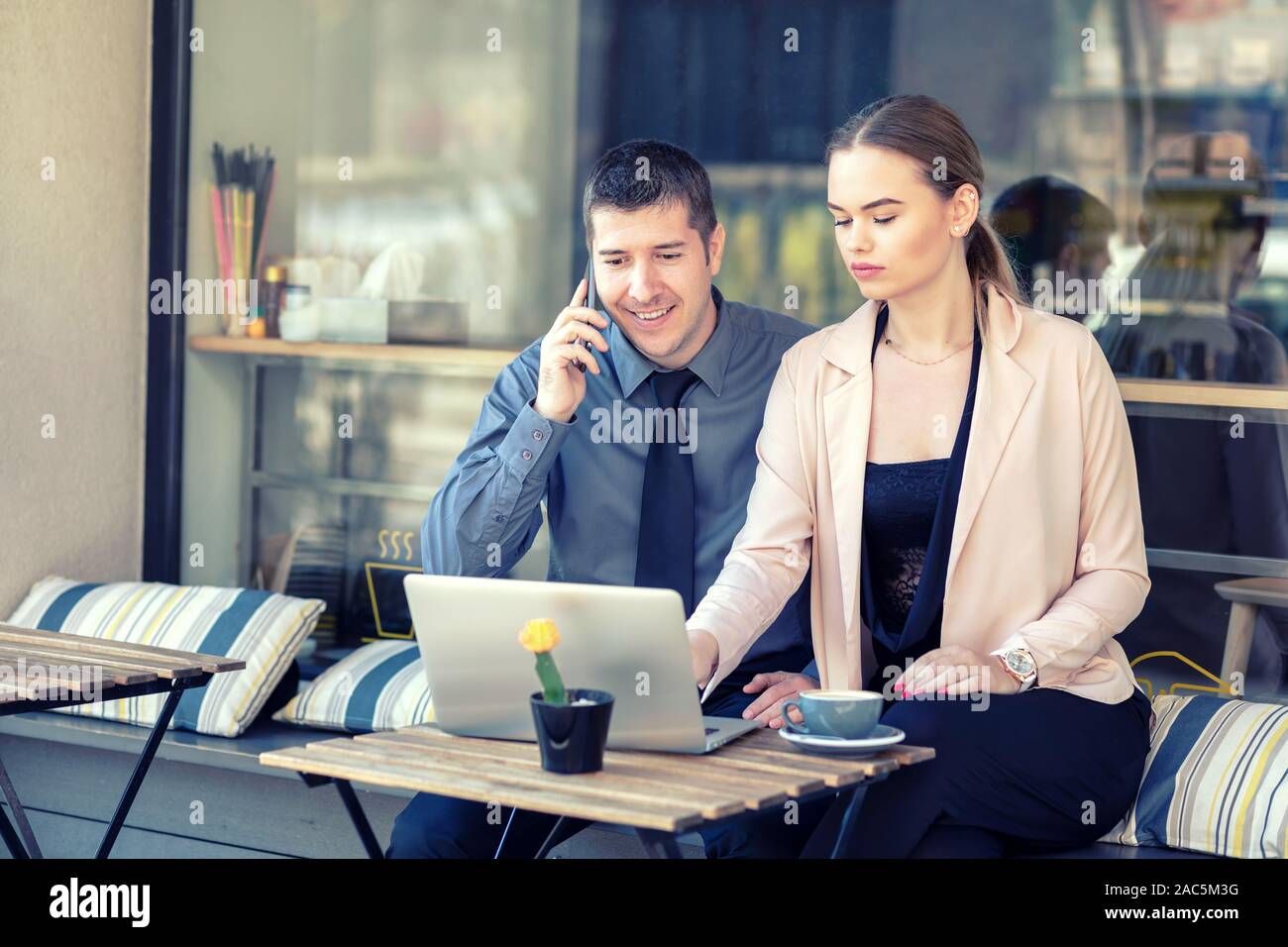 Smiling business people using laptop at cafe terrace while talking on ...