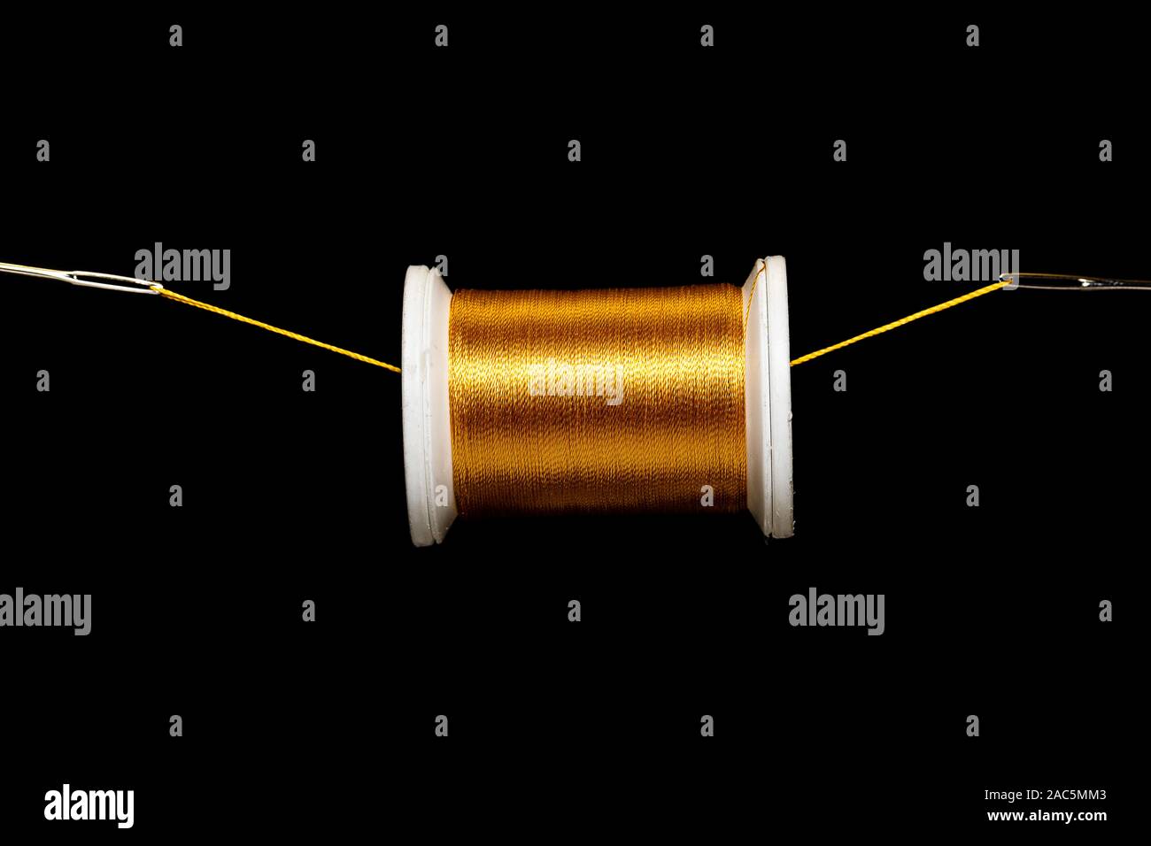 A spool of gold thread suspended on a field of black on a thread ...