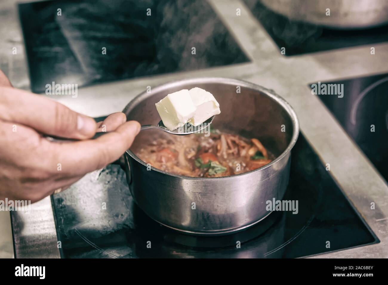 Chef is adding pieces of butter to a dish cooking on electric induction ...