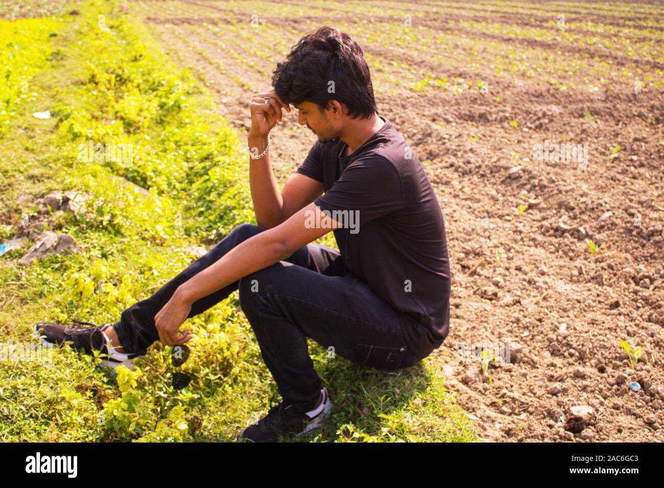 A young boy is sitting on field and thinking deeply or in tension ...