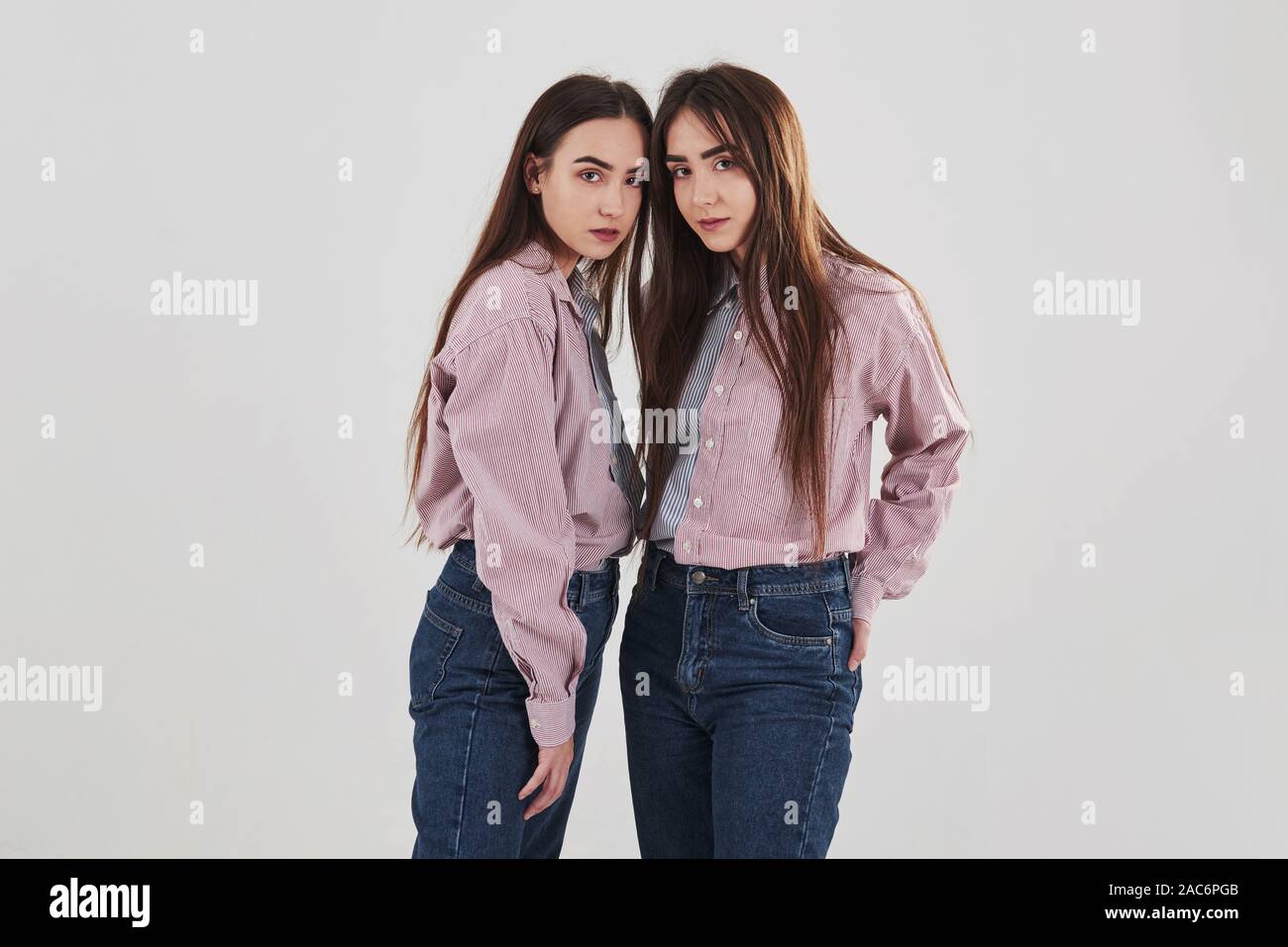 Always together. Two sisters twins standing and posing in the studio ...