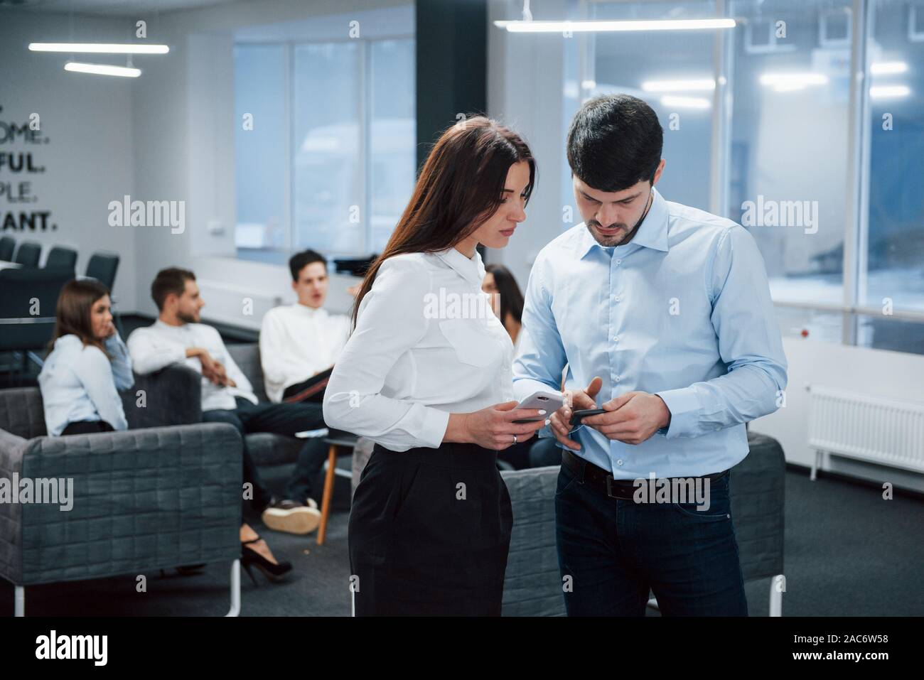 Using smartphones. Two office workers in classic clothes talking in ...