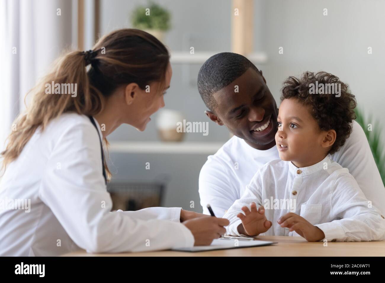 Cheerful young female pediatrician and black father listening to ...