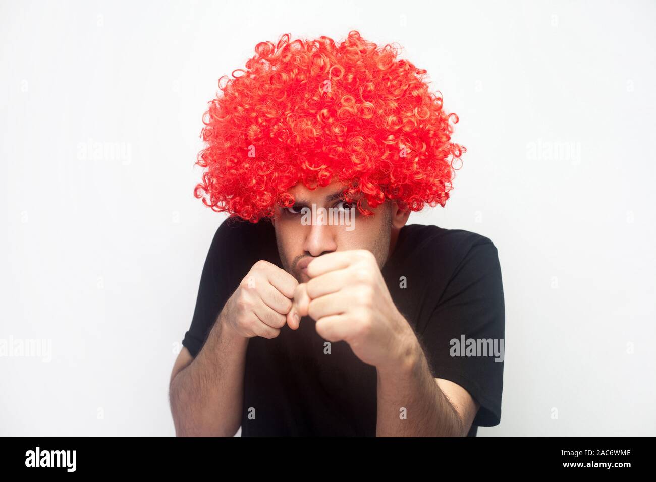 Portrait of funny man with bristle and curly red wig clenching fists in ...