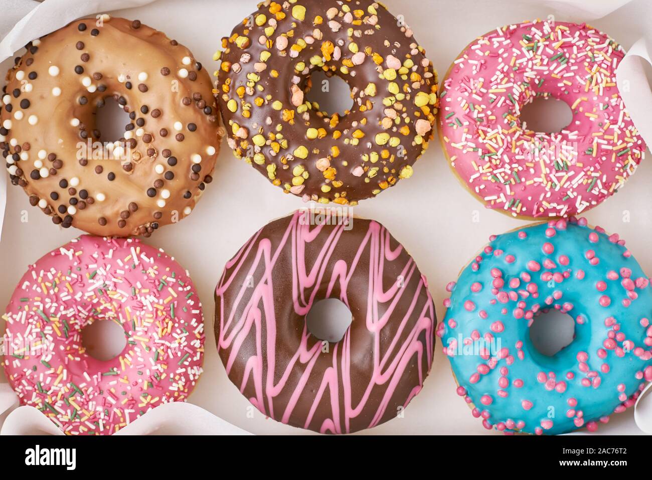 Different types of colorful donats decorated sprinkles and icing in box ...