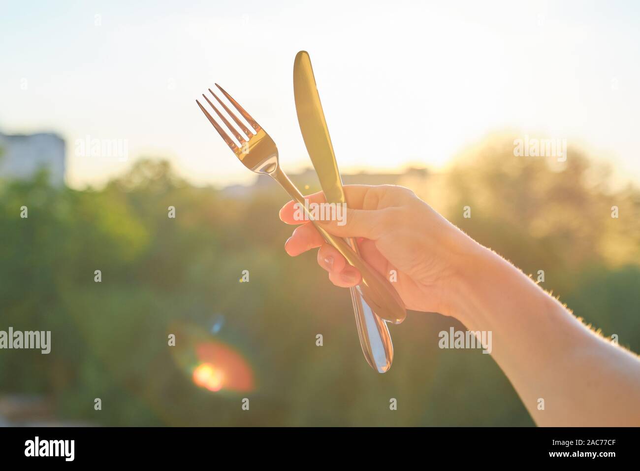 Steel metal shiny knife and fork in a womans hand, background sunset ...