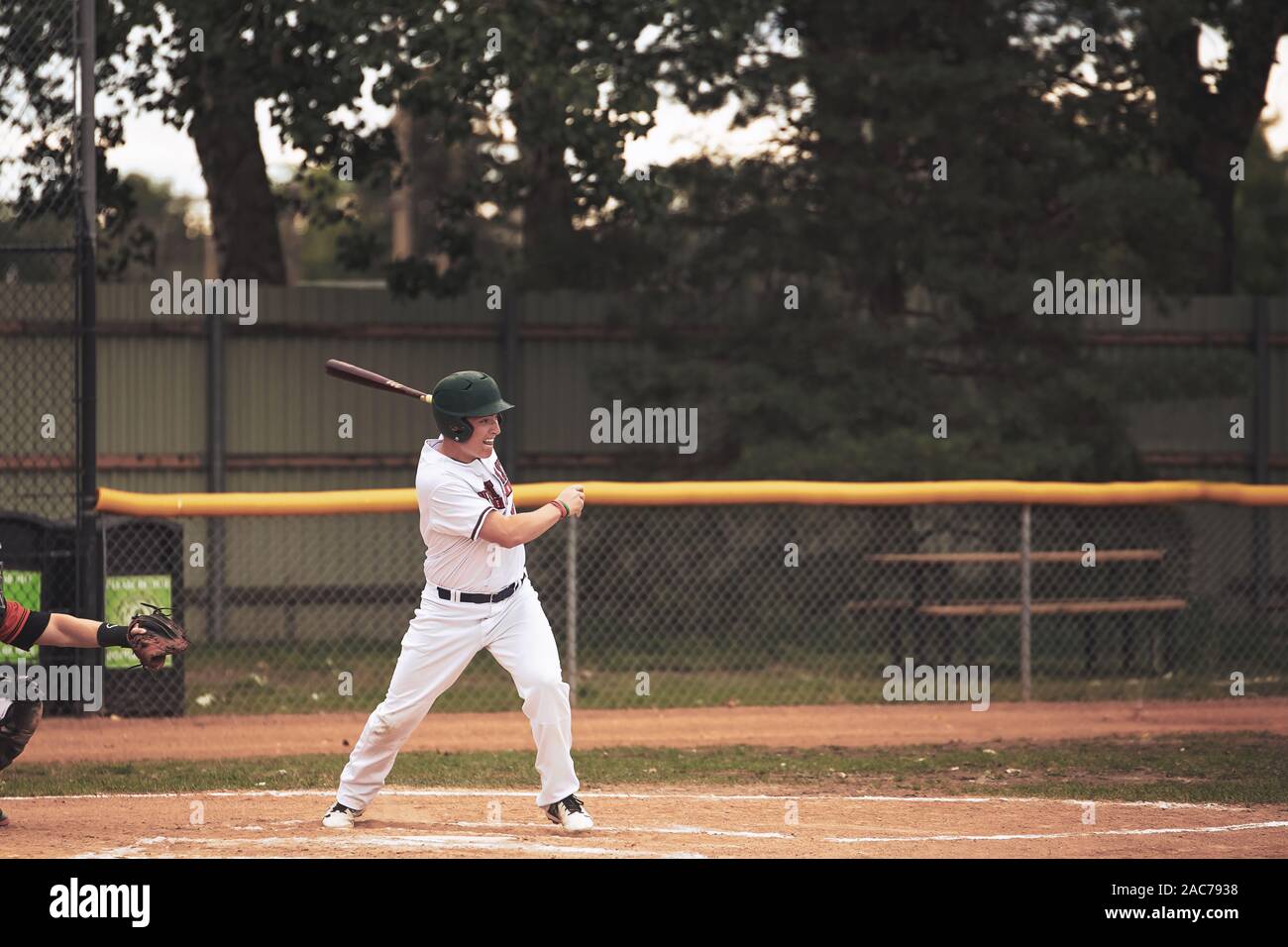 An eighteen year old male swinging the bat at home plate in a white and ...