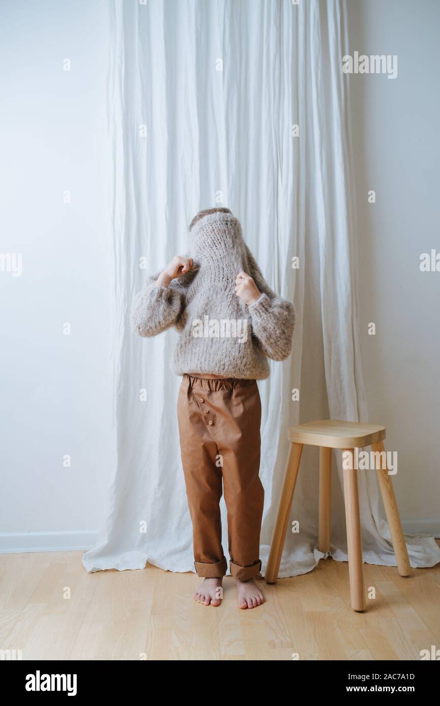 Little girl putting on sweater, she pulled it over head, looking ...