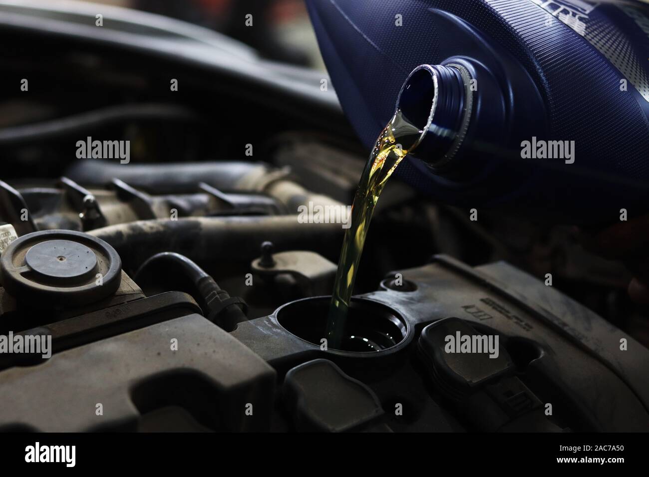 Mechanic pours motor oil into engine from blue plastic container Stock ...