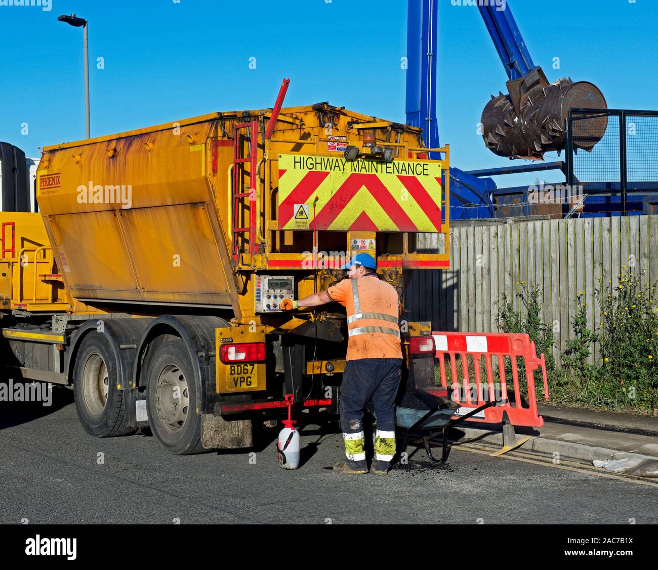 Workman loading Tarmac into wheelbarrow, for repairs to road surface ...