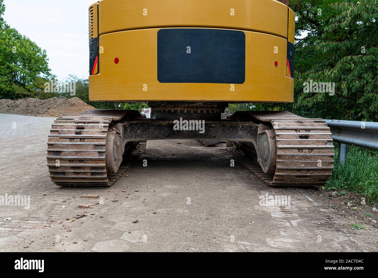 A large yellow excavator visible from the rear, standing on concrete ...