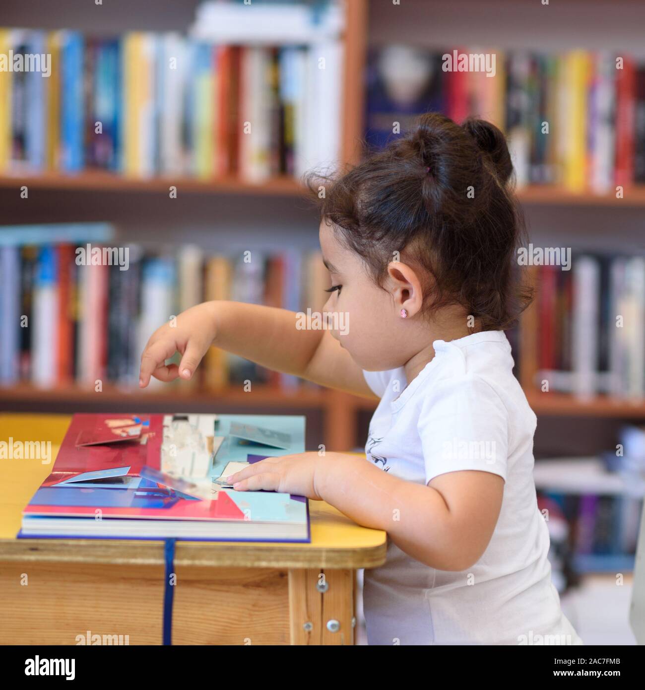 Little Girl Indoors In Front Of Books. Cute Young Toddler Sitting On A ...