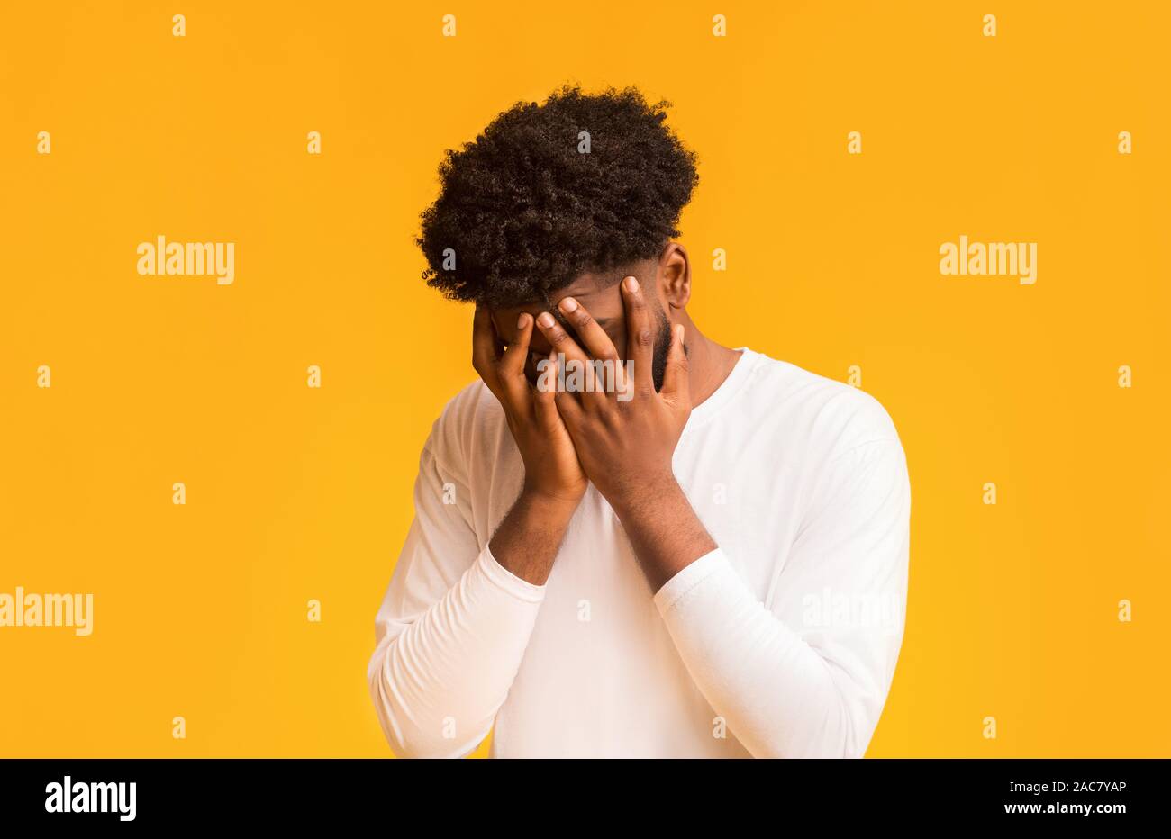 Young afro guy covering his face with both hands Stock Photo - Alamy