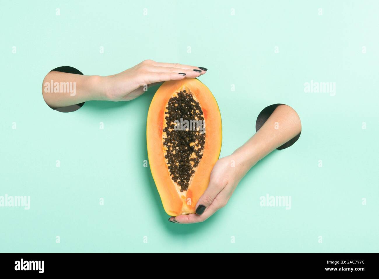 Female hands hold fresh papaya through a hole on neon mint background ...