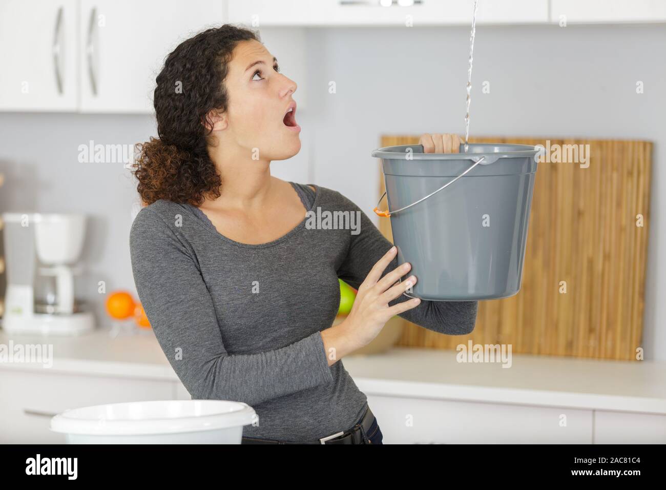 woman holding bucket while water droplets leak from ceiling Stock Photo ...