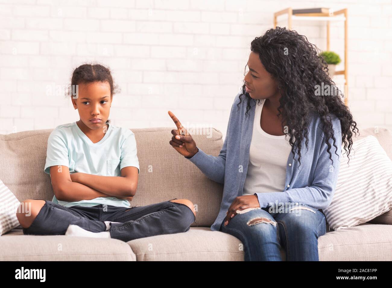 Grumpy black mother scolding her naughty little daughter on sofa at ...