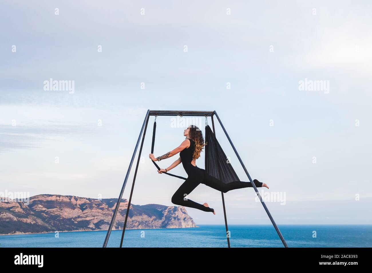 Woman practice acrobatic fly dance yoga outdoors with sea and mountain ...