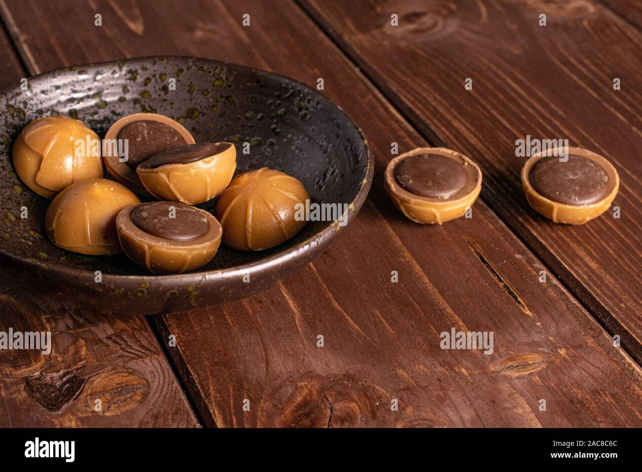 Group of eight whole sweet brown toffee in glazed bowl on brown wood ...
