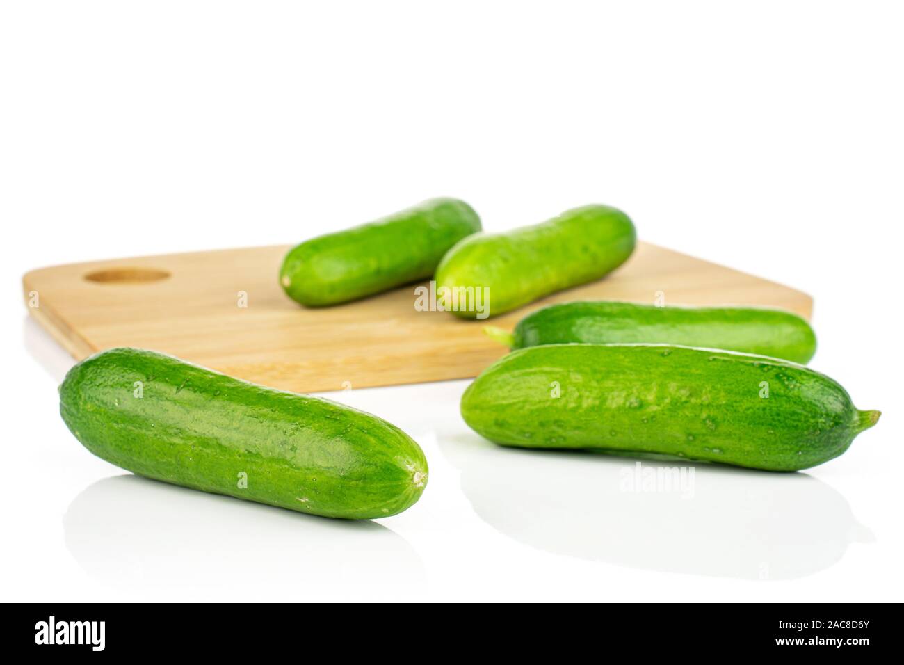 Group of five whole fresh green baby cucumber on bamboo cutting board ...