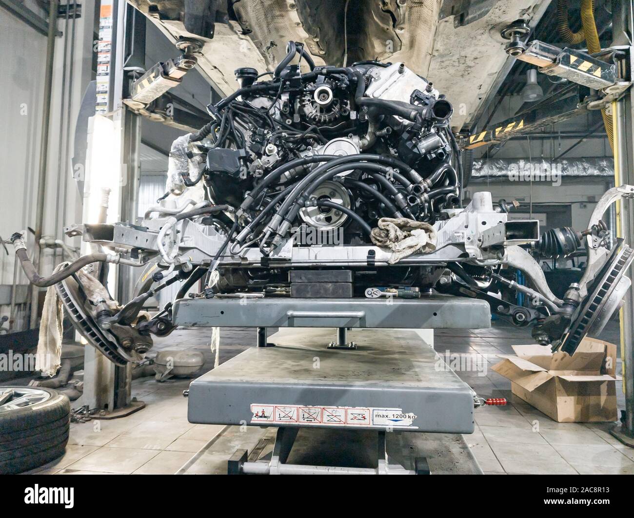 A used car raised on a lift for repair and under it a detached engine ...