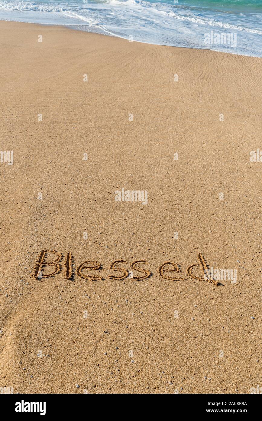The word Blessed written in the sand on the beach with a wave washing ...