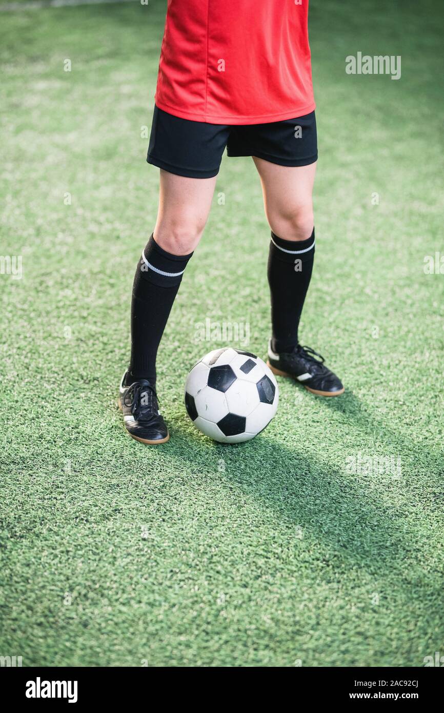 Soccer ball between legs of active girl in sports uniform standing on ...