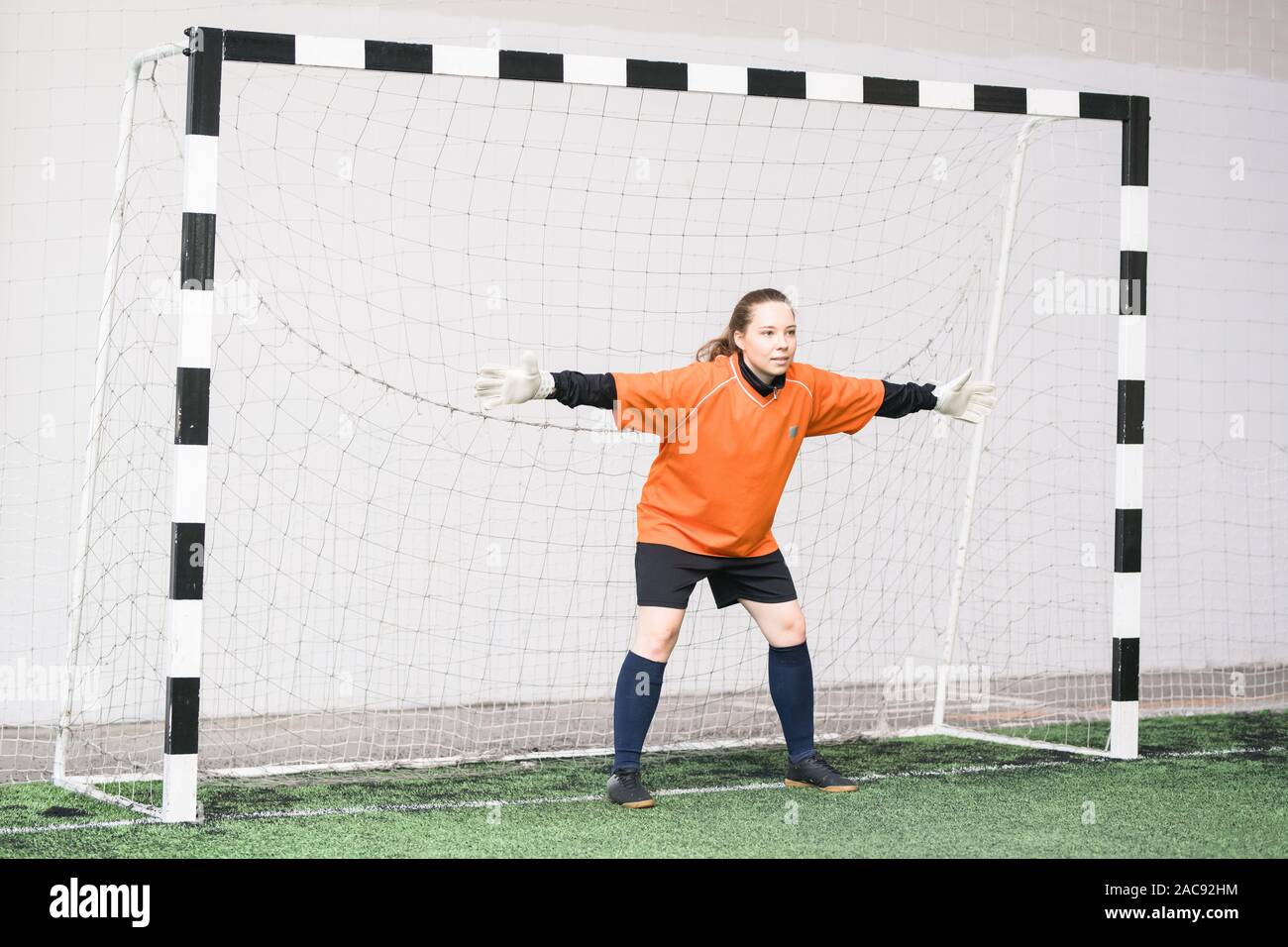 Young female goal keeper in sports uniform and gloves outsretching her ...