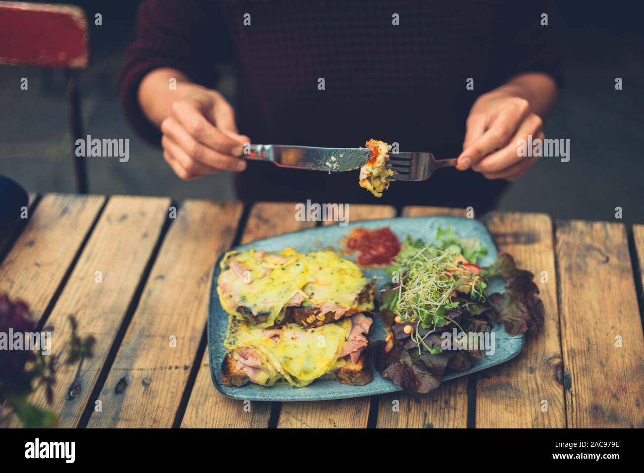 A young woman is eating an open sandwich with cheese and ham in a cafe ...