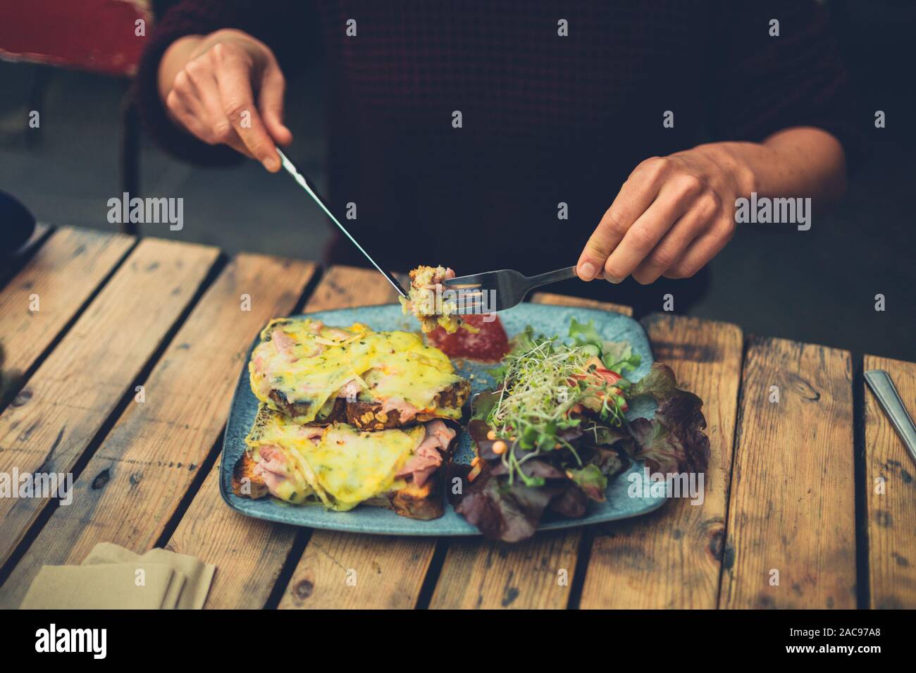 A young woman is eating an open sandwich with cheese and ham in a cafe ...