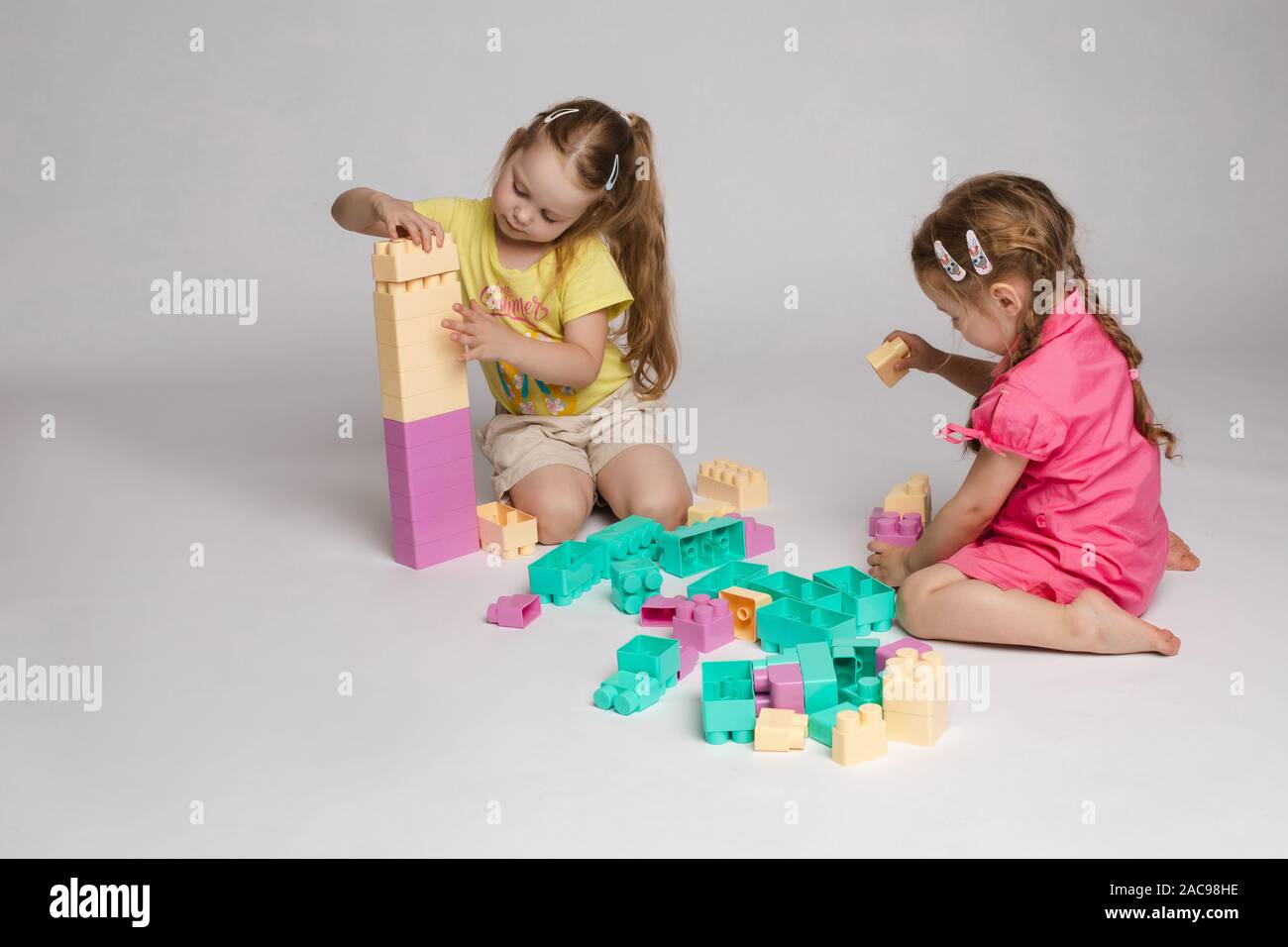 Two enthusiastic little girl playing assemble constructor full shot at ...