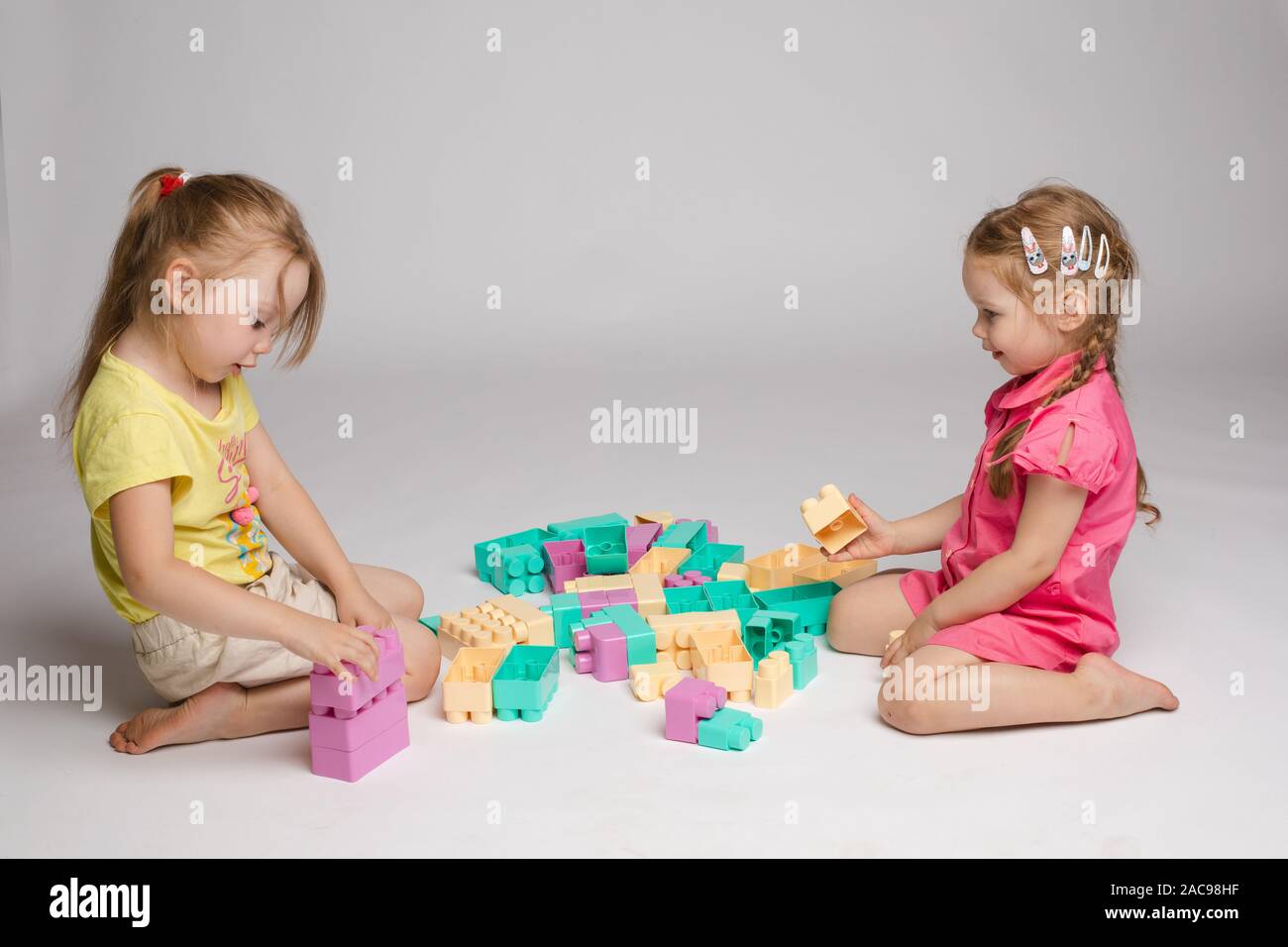 Two enthusiastic little girl playing assemble constructor full shot at ...