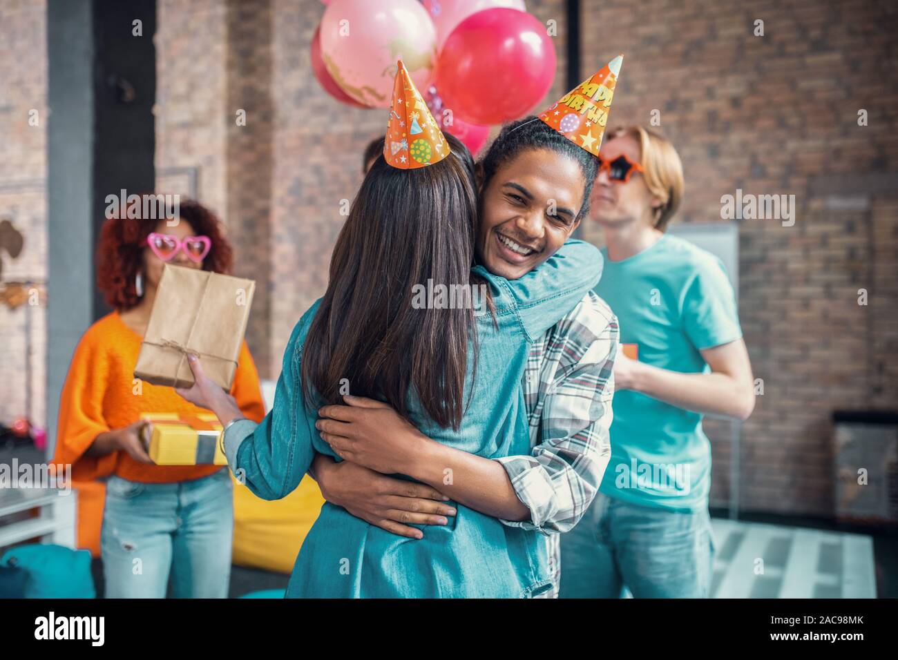 Hugging birthday girl. Dark-skinned smiling boyfriend hugging his ...