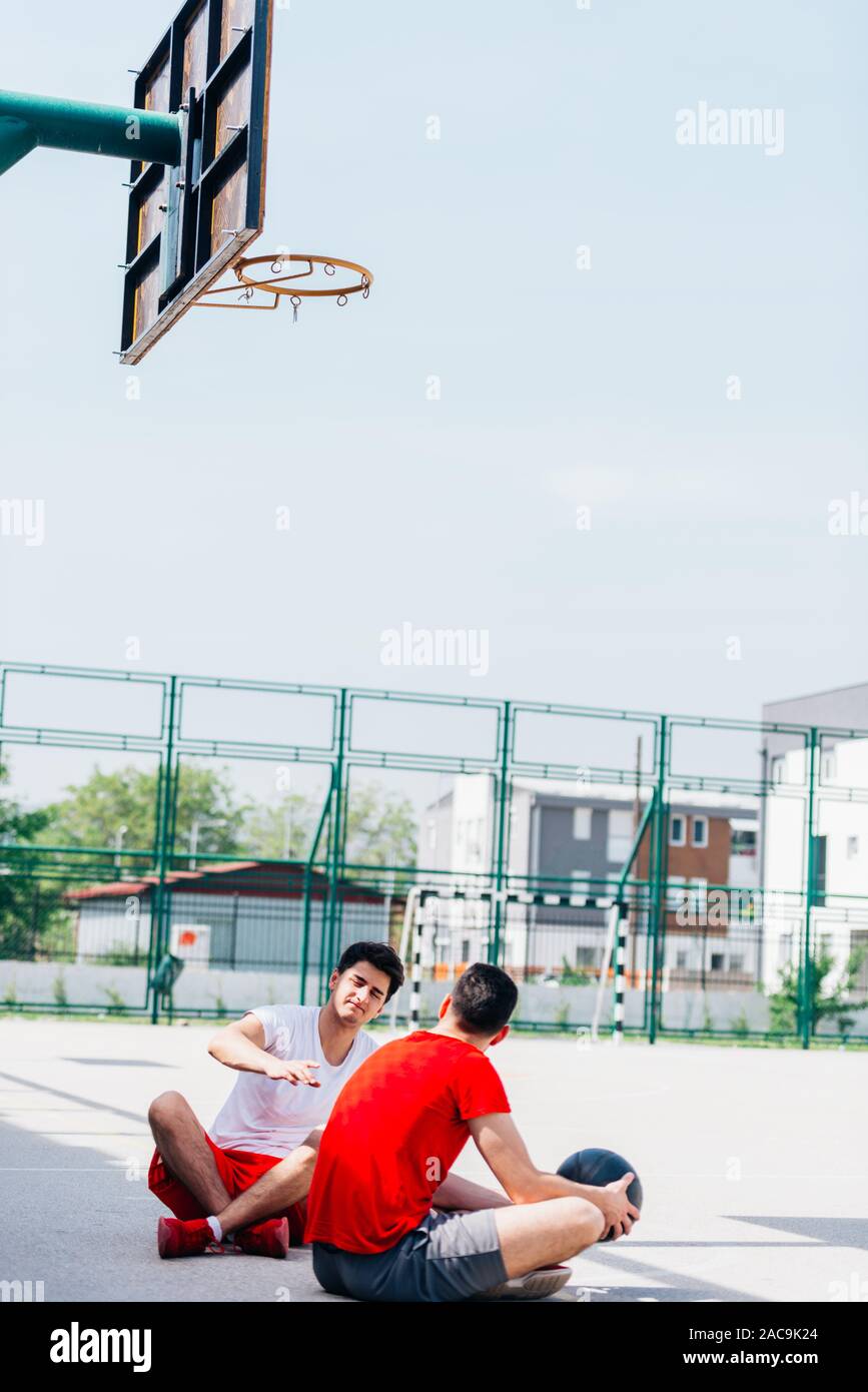 Two strong caucasian athletes resting on the ground at the basketball ...