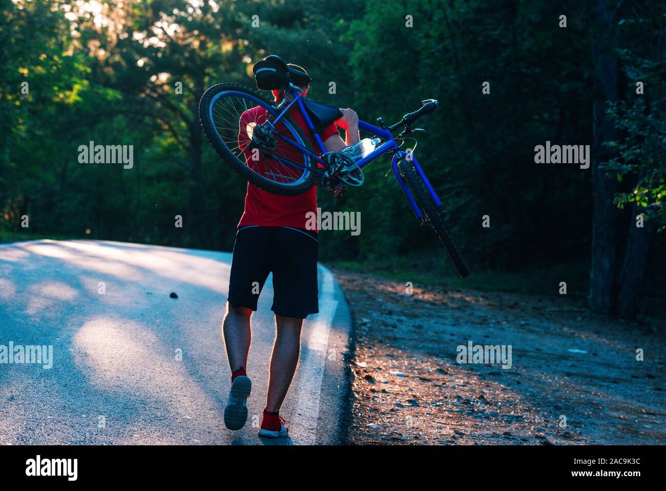 Strong athlete cyclist ( biker ) carrying his bicycle on his back on an ...