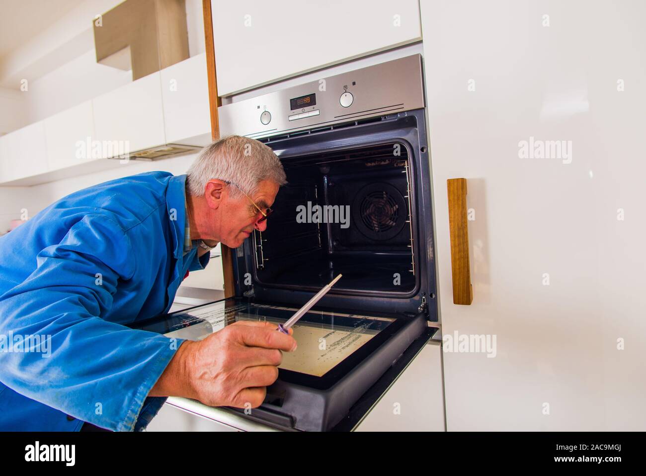 Mature handyman is working in the kitchen, fixing the oven Stock Photo ...